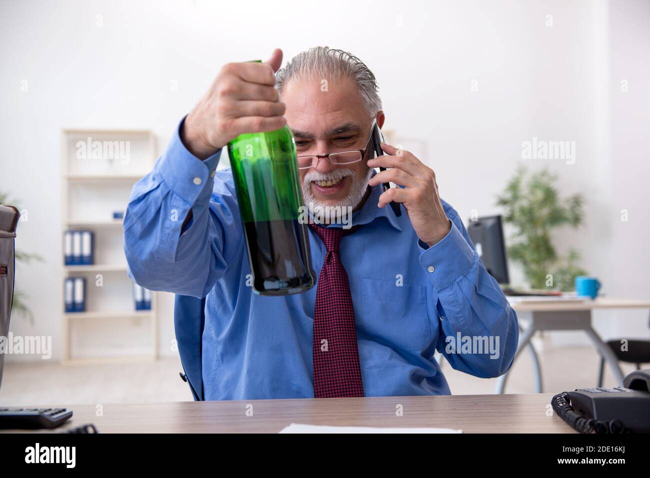 Senior male employee drinking alcohol in the office Stock Photo - Alamy