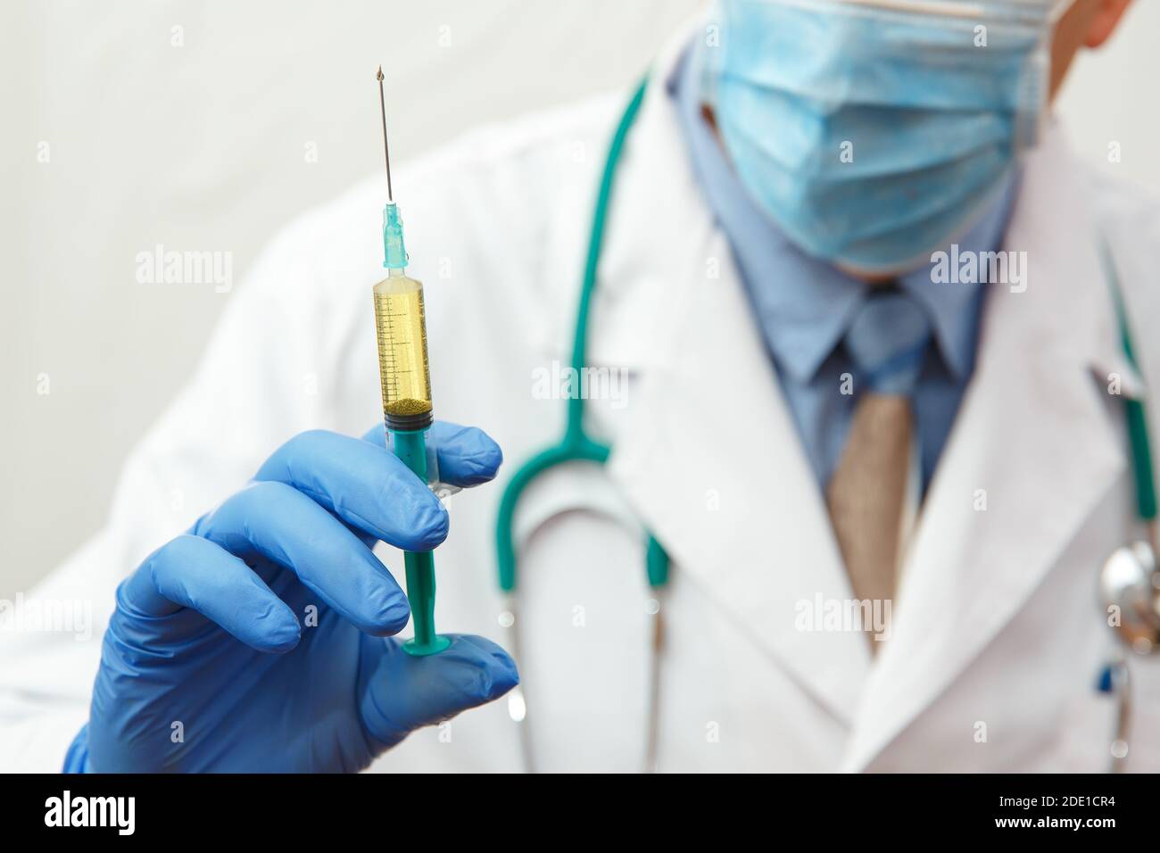 Doctor in mask holding a medical injection syringe and stethoscope ...