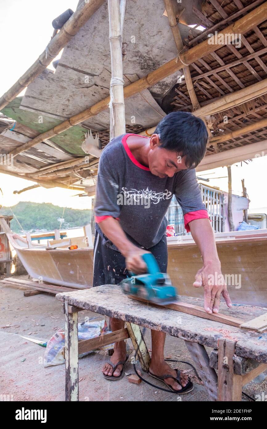 A Filipino wood worker working on a piece of wood for his boat being ...