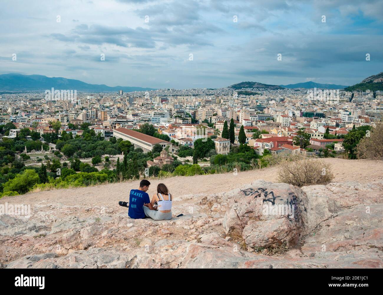 Two young people sitting on the Areopagus hill overlooking modern ...