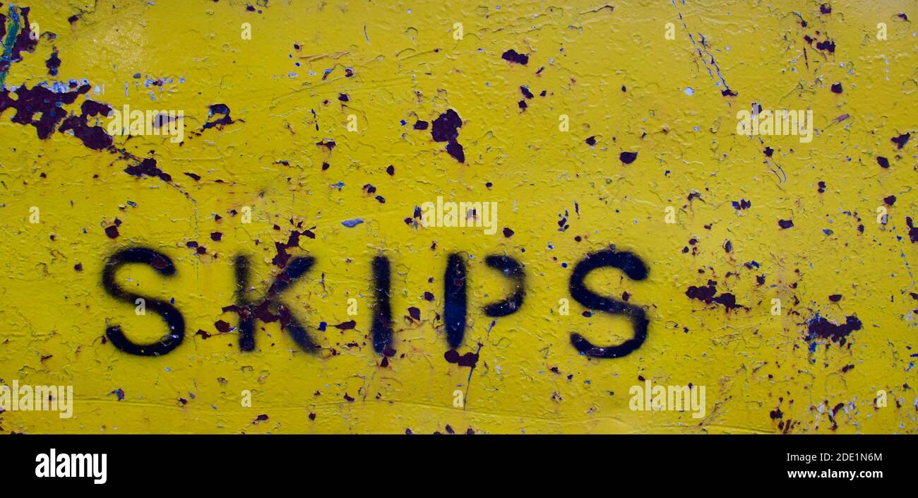 The word skips stencilled onto rusting yellow metal with copy space ...