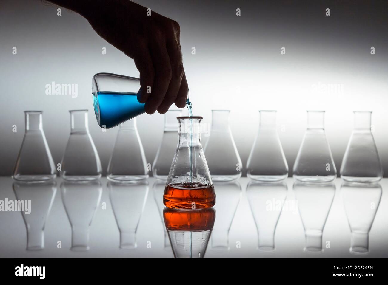 Hand pouring blue in to red liquid in scientific laboratory glass ...