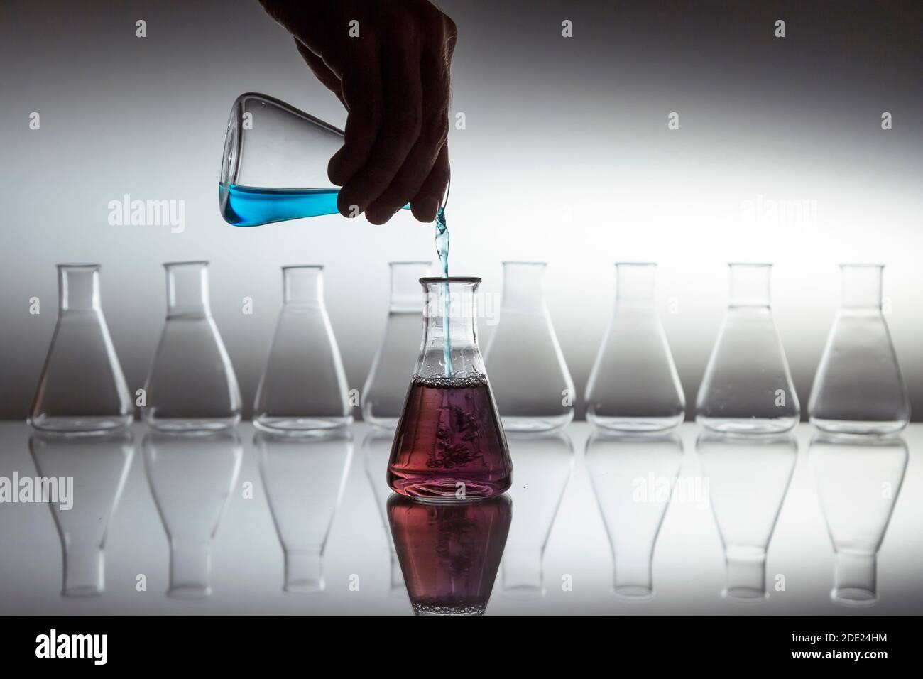 Hand pouring blue in to red liquid in scientific laboratory glass ...
