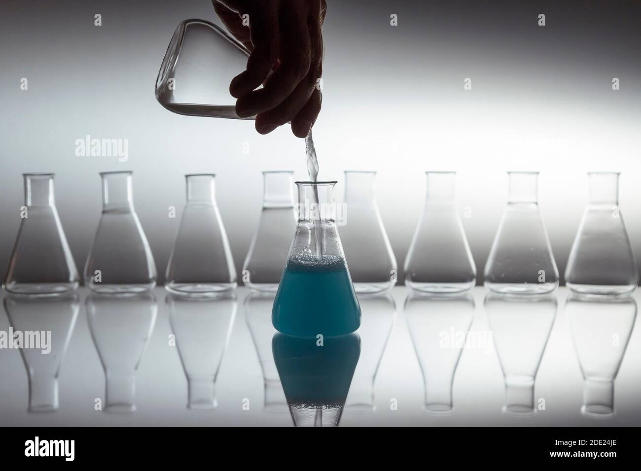 Hand pouring white in to blue liquid in scientific laboratory glass ...
