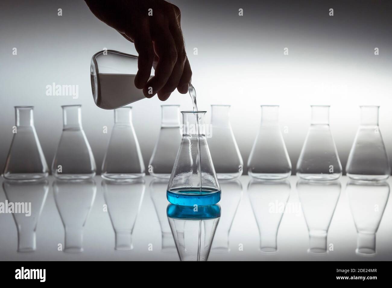 Hand pouring white in to blue liquid in scientific laboratory glass ...