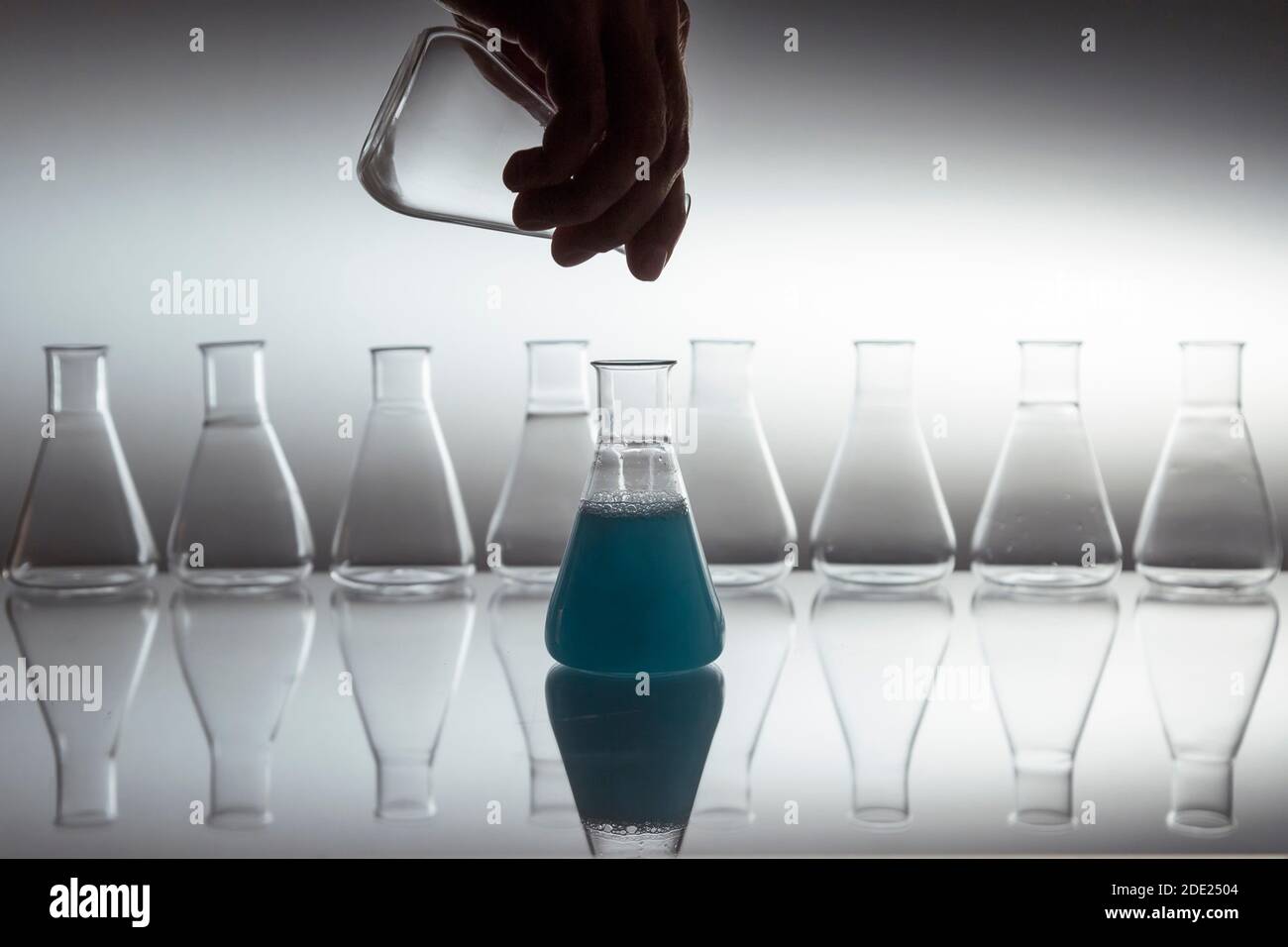 Hand pouring white in to blue liquid in scientific laboratory glass ...