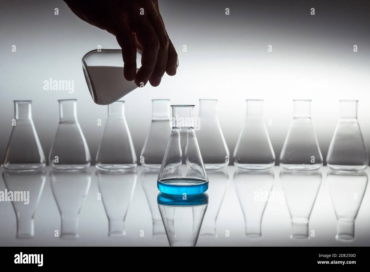 Hand pouring white in to blue liquid in scientific laboratory glass ...