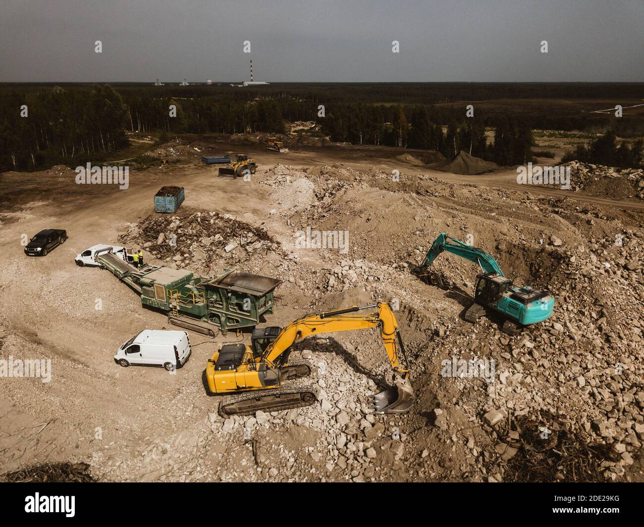 Aerial photo. Excavators and tractors at construction site near forest. Earthmoving at open pit ...