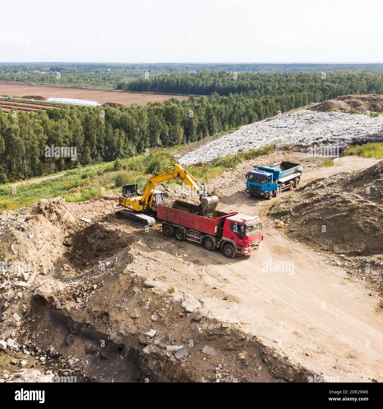 Heavy excavator in action. Trucks on dirt road. Construction works near ...