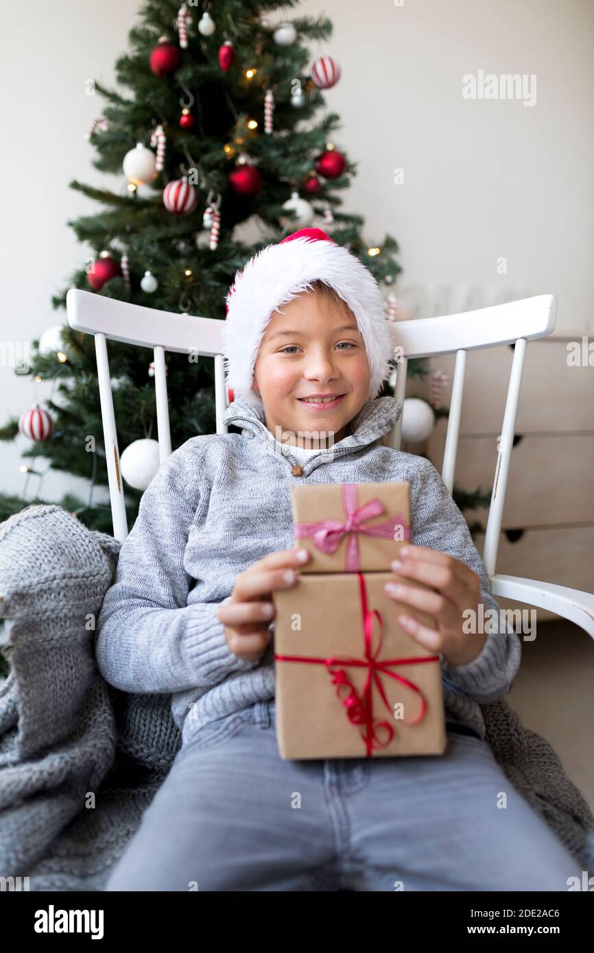 Young boy in santa clause hat in front of a Christmas tree with ...