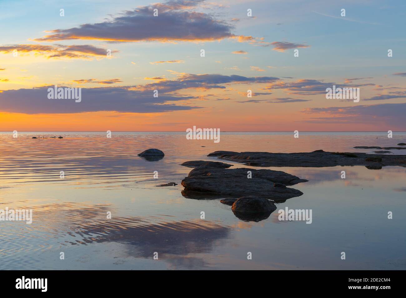 Beautiful colorfull sunset over the sea shore with rocks under shallow ...