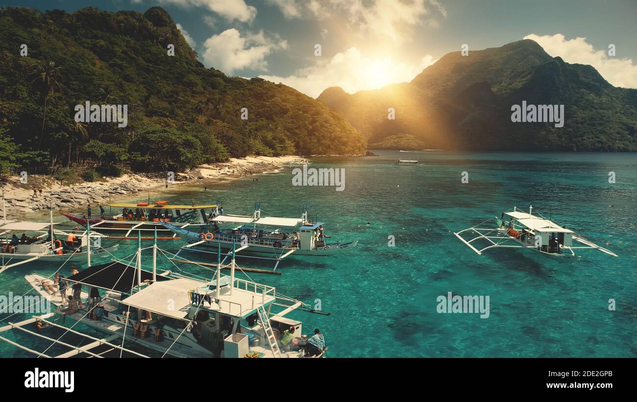 Sun over mountain ranges with green tropic forest at ocean bay. People ...