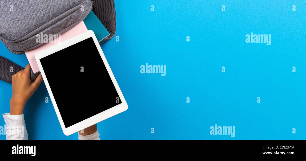 Kid hands taking digital tablet computer from gray backpack over light ...
