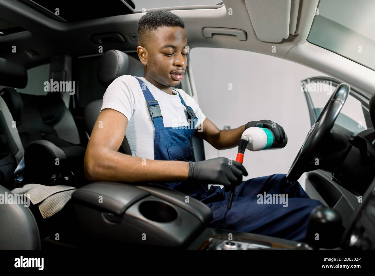 Portrait of young African male car detailing worker, sitting inside of ...