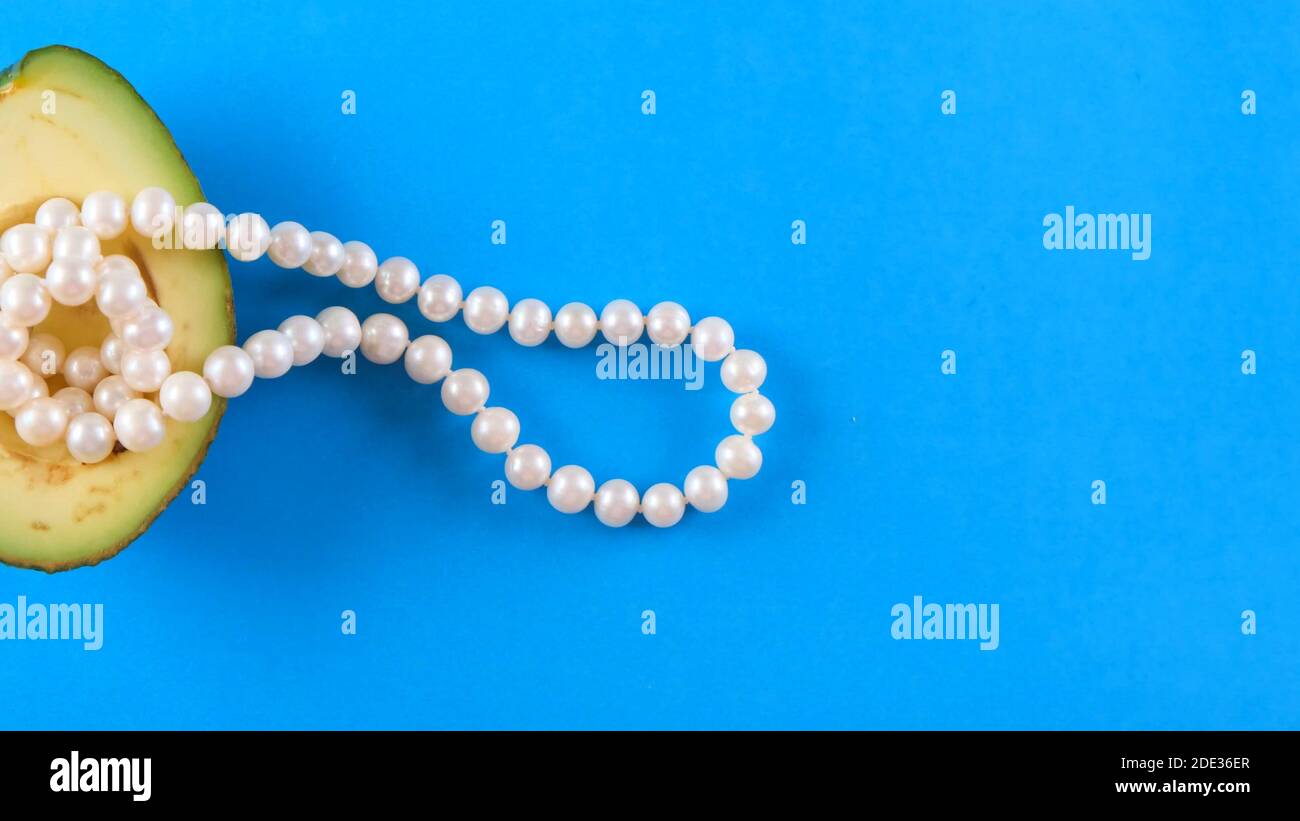 Half fresh avocado fruit with pearls on blue background. Fashionable ...