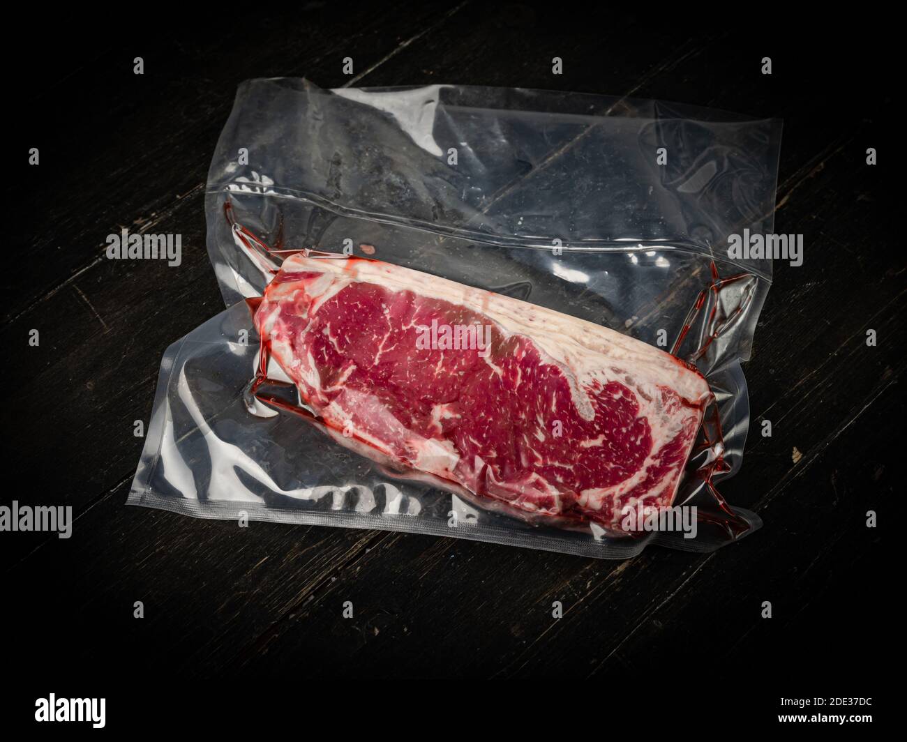 Vacuum-packed raw ribeye beef steak in the wood background. Top view ...