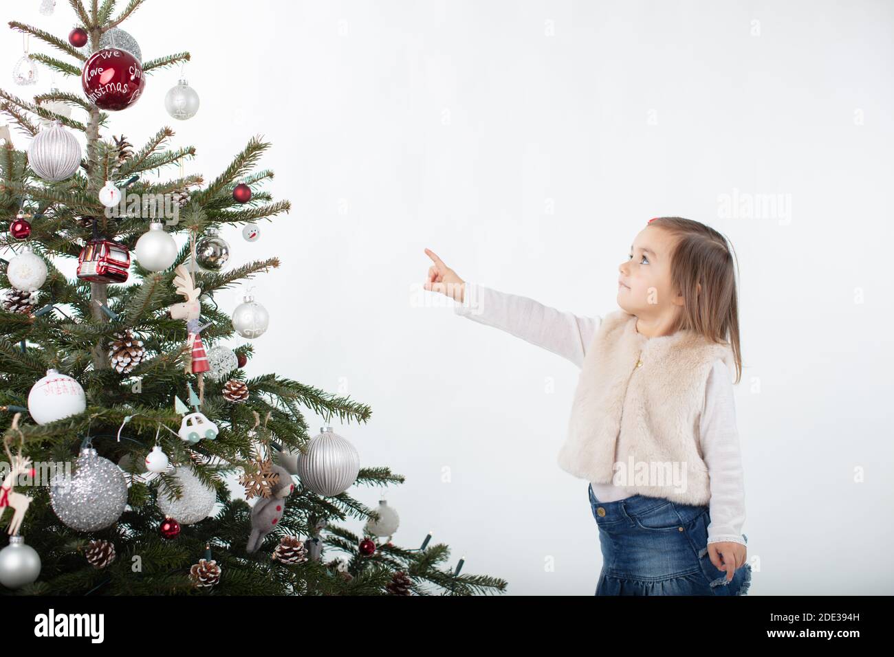 A toddler girl pointing towards the tip of the Christmas tree Stock ...