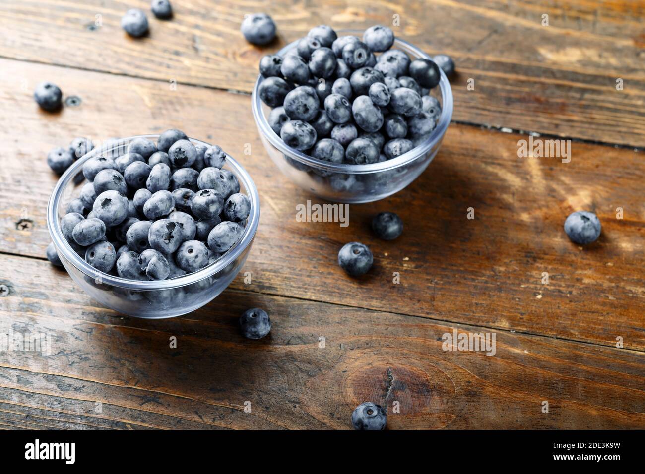 Fresh blueberries in a glass bowl and scattered on a wooden table ...