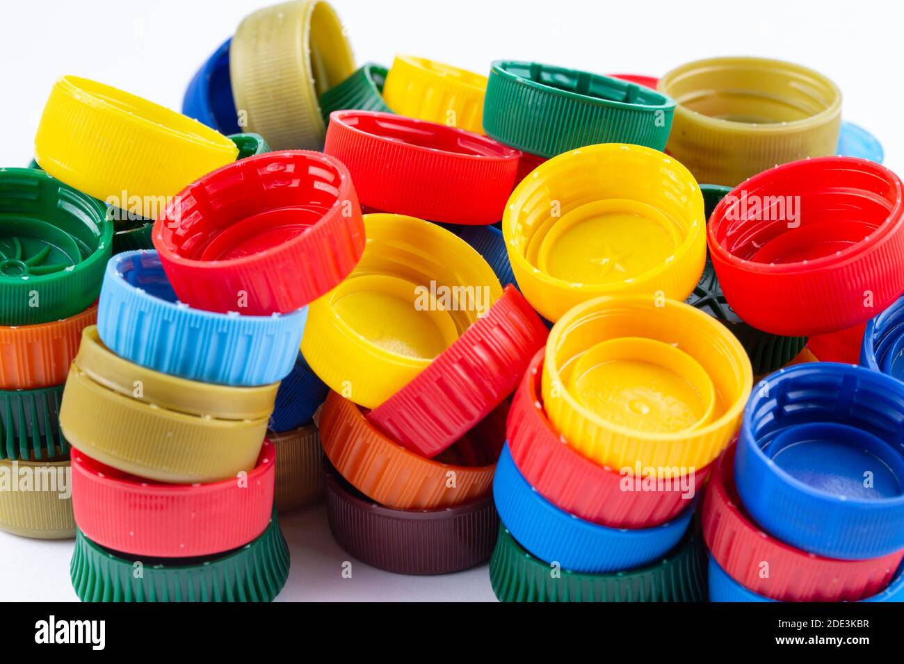 Many multi-colored plastic bottle caps on a white background. Recycling ...