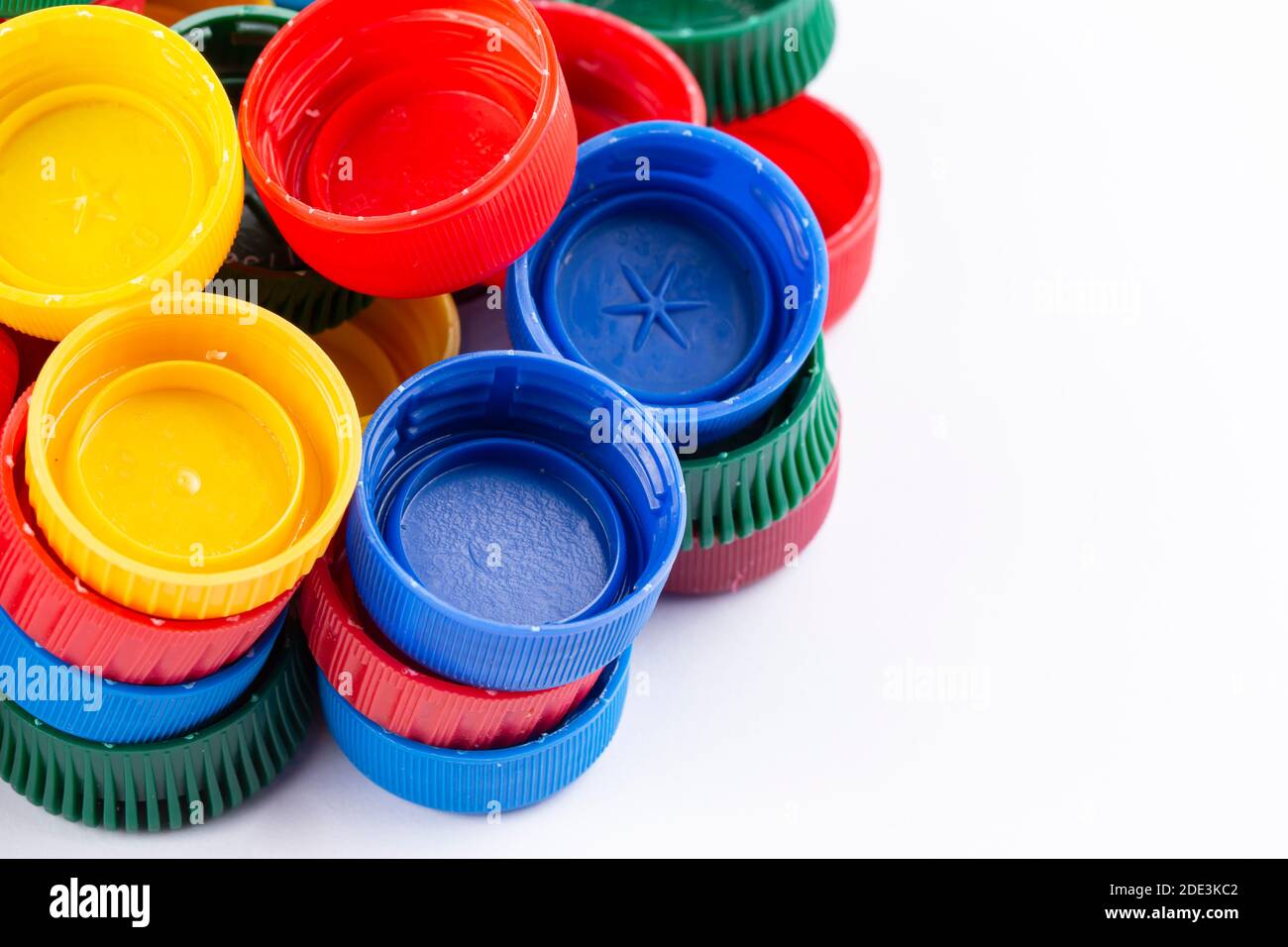 Many multi-colored plastic bottle caps on a white background. Recycling ...