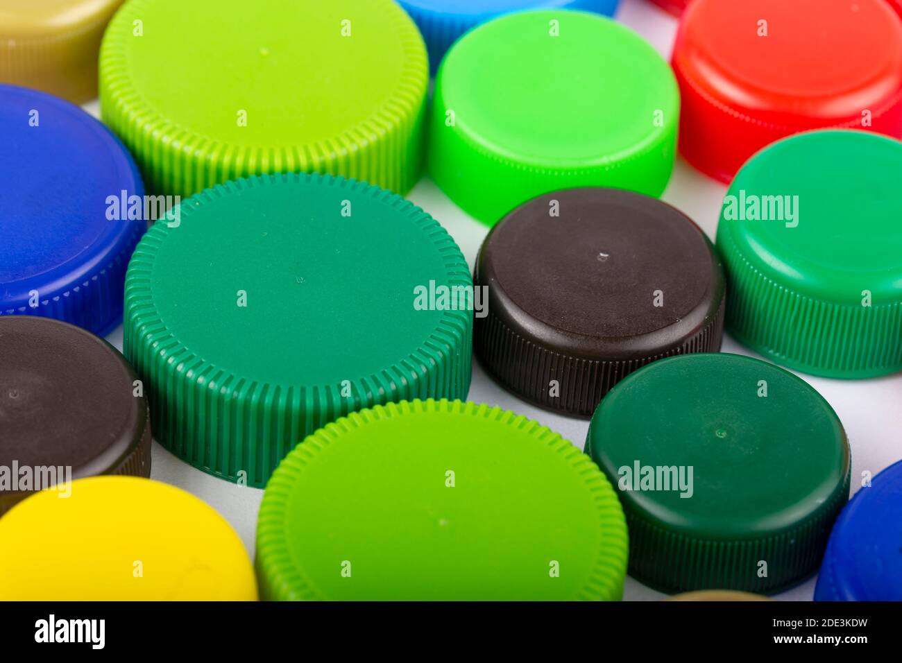 Many multi-colored plastic bottle caps on a white background. Recycling ...