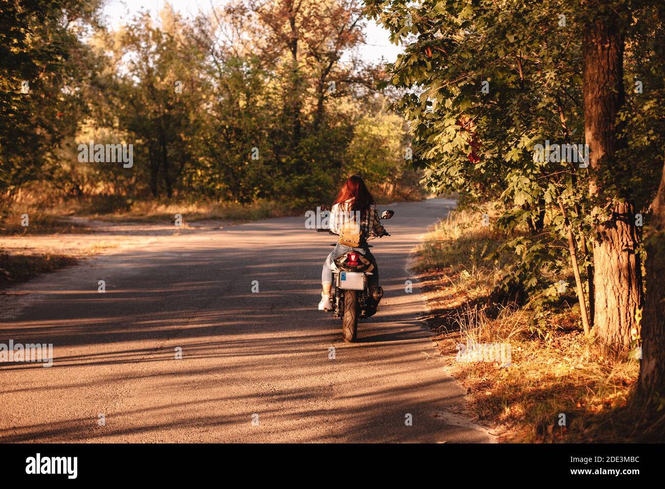 Back view of woman riding motorcycle on country road amidst trees Stock ...