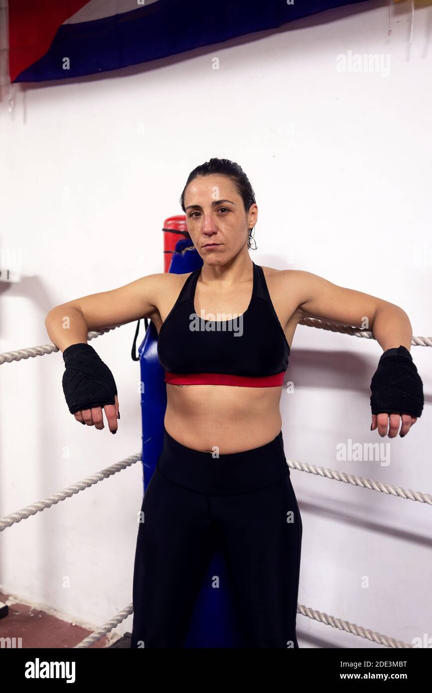 Real female boxer in gloves leaning on rope at ring before training ...