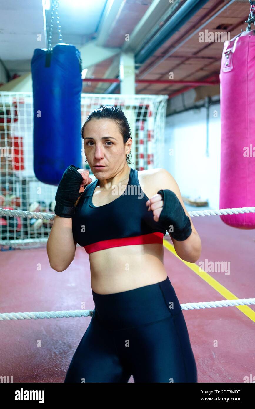 Real female boxer in gloves leaning on rope at ring before training ...