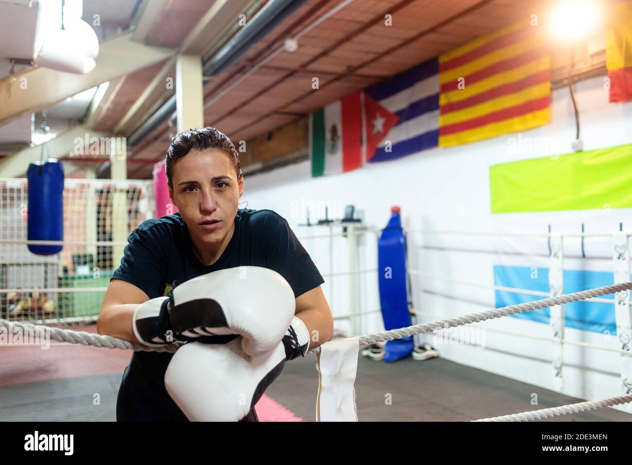 Real female boxer in gloves leaning on rope at ring before training ...