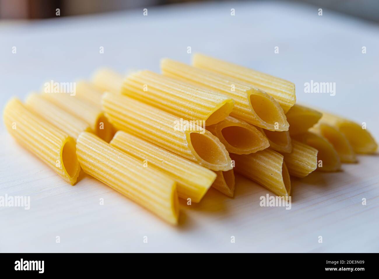 Raw penne rigate on white surface. Pasta, preparation, and price Stock ...