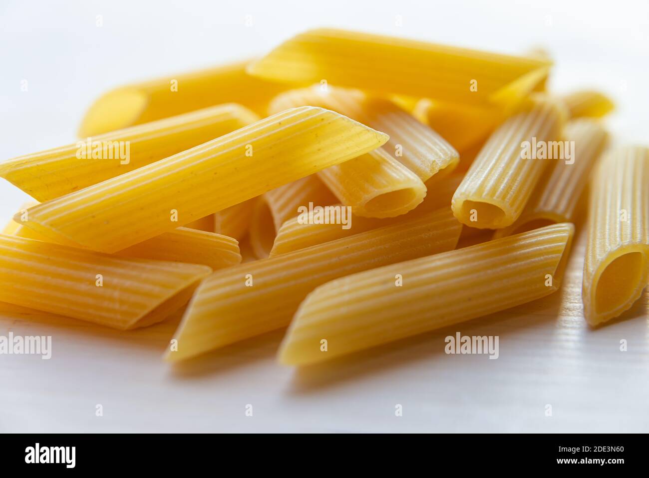 Raw penne rigate on white surface. Pasta, preparation, and price Stock ...