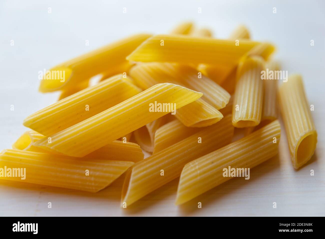 Raw penne rigate on white surface. Pasta, preparation, and price Stock ...