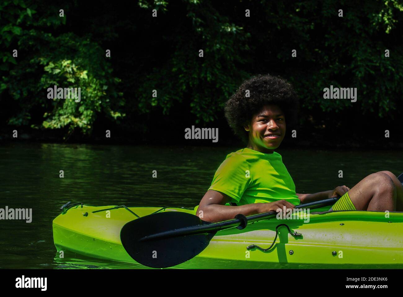 Happy teenager kayaking with paddle on scenic river with copy space ...