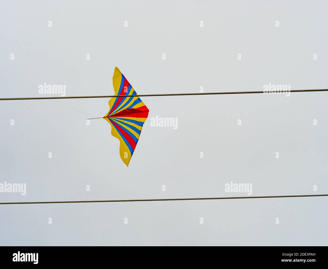 Red striped yellow kite stuck on electrical wires. Autumnal gray sky ...