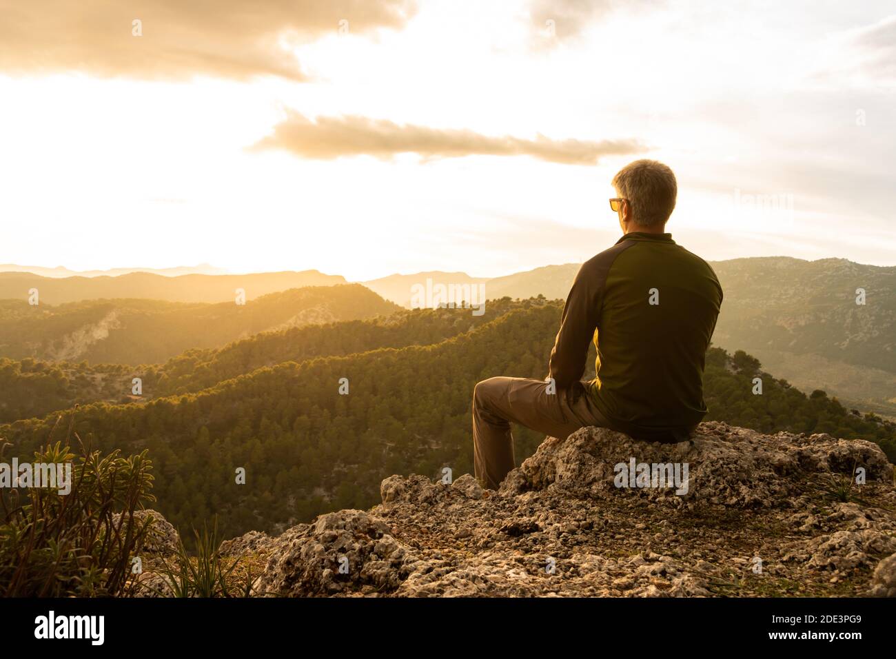 A man alone contemplates the sunset sitting on a rock from the top of a ...