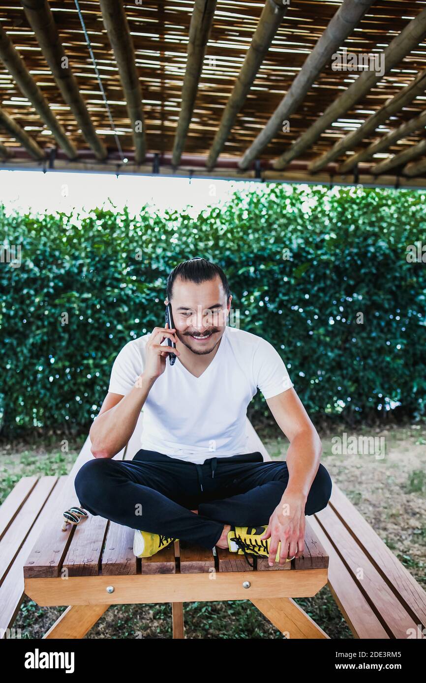Mexican Man using smartphone sitting cross-legged, Home work and ...