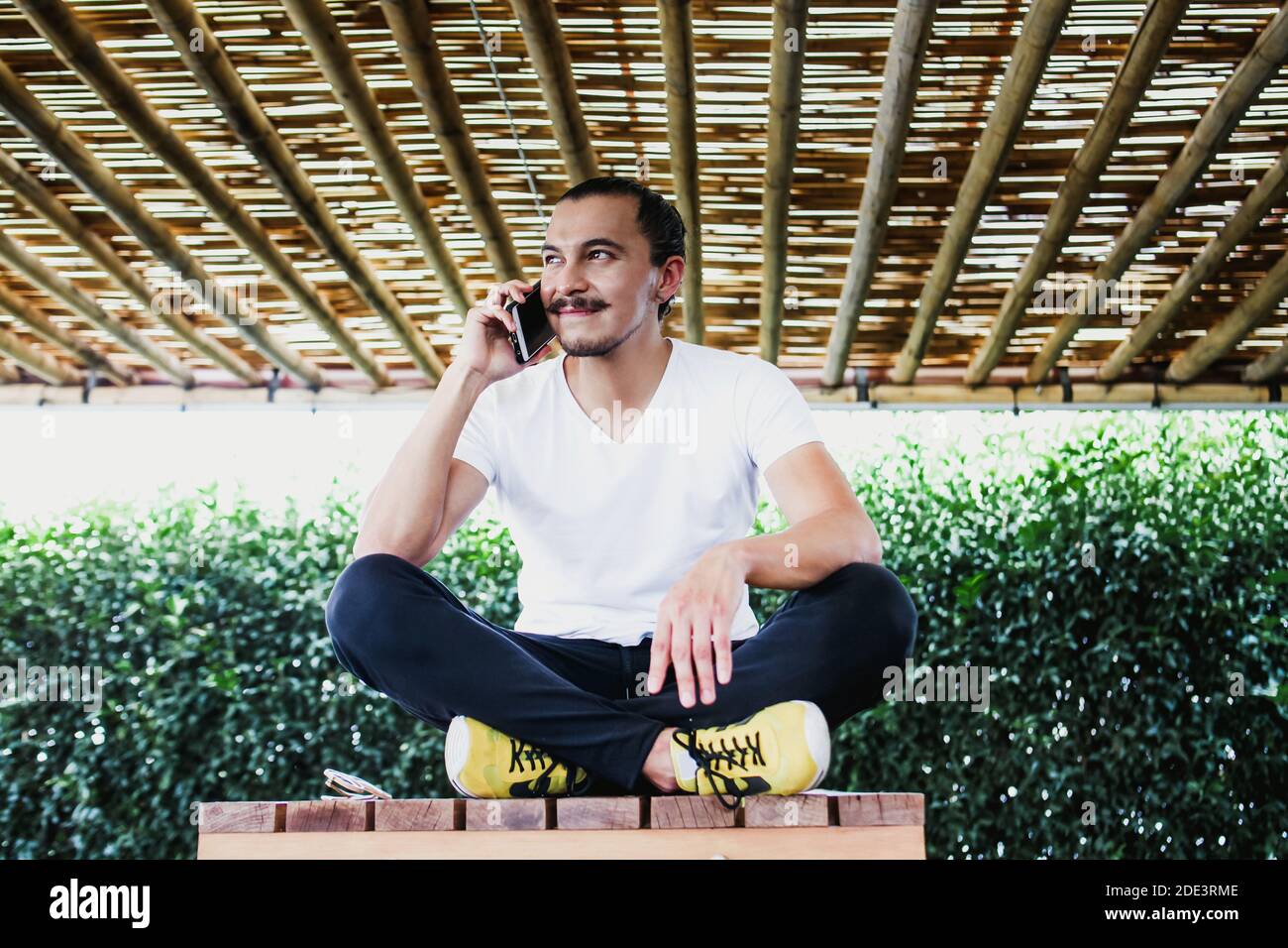 Mexican Man using smartphone sitting cross-legged, Home work and ...