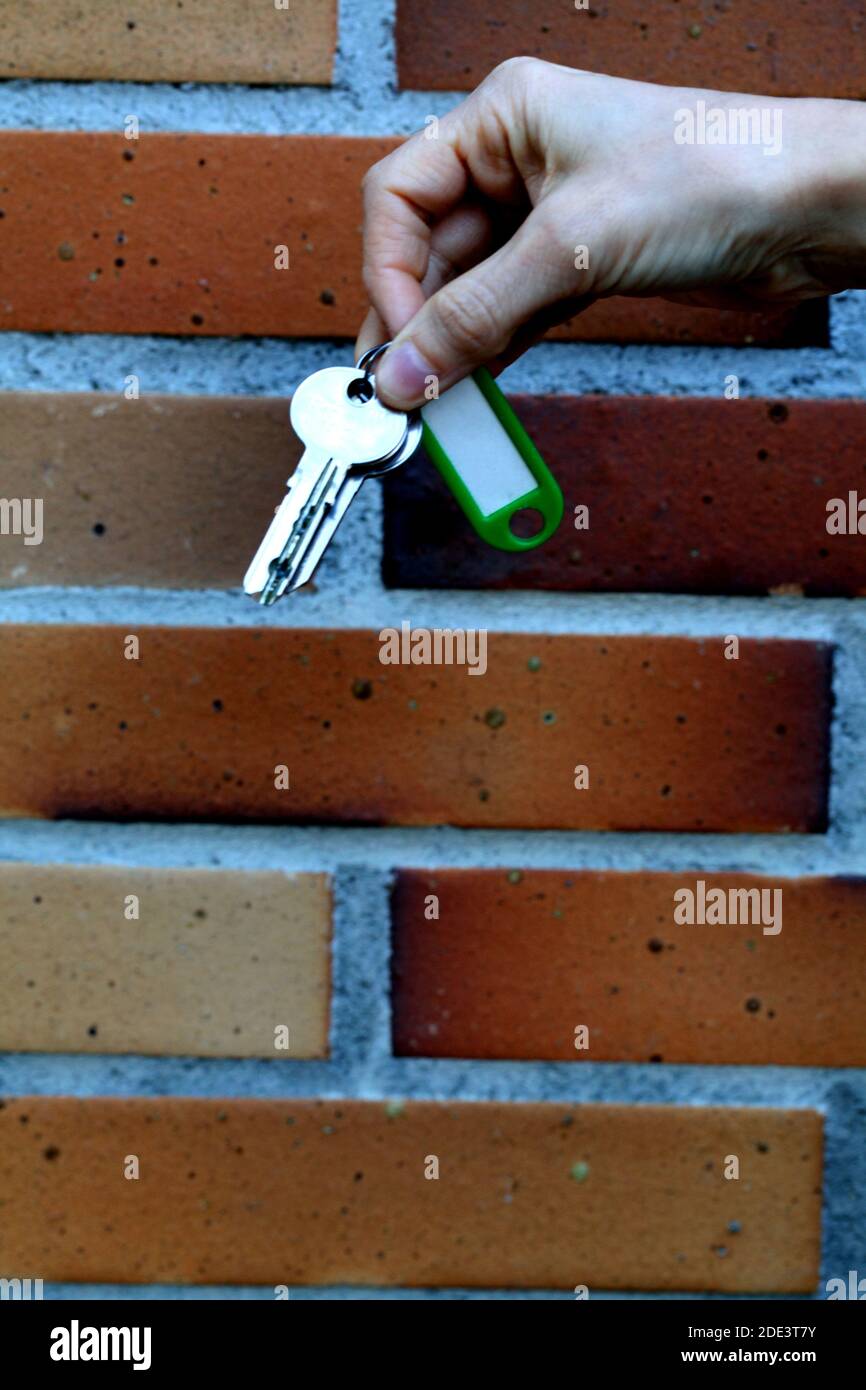 A hand holding keys with a keychain on a brick wall background Stock ...