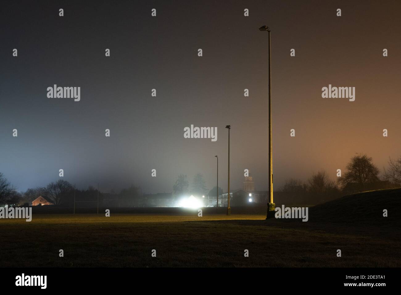 An empty sports field with flood lights on a moody foggy winters night ...