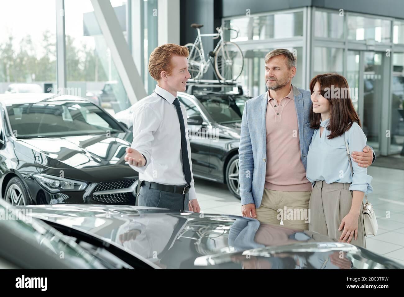 Confident young sales manager of modern auto center showing one of new ...