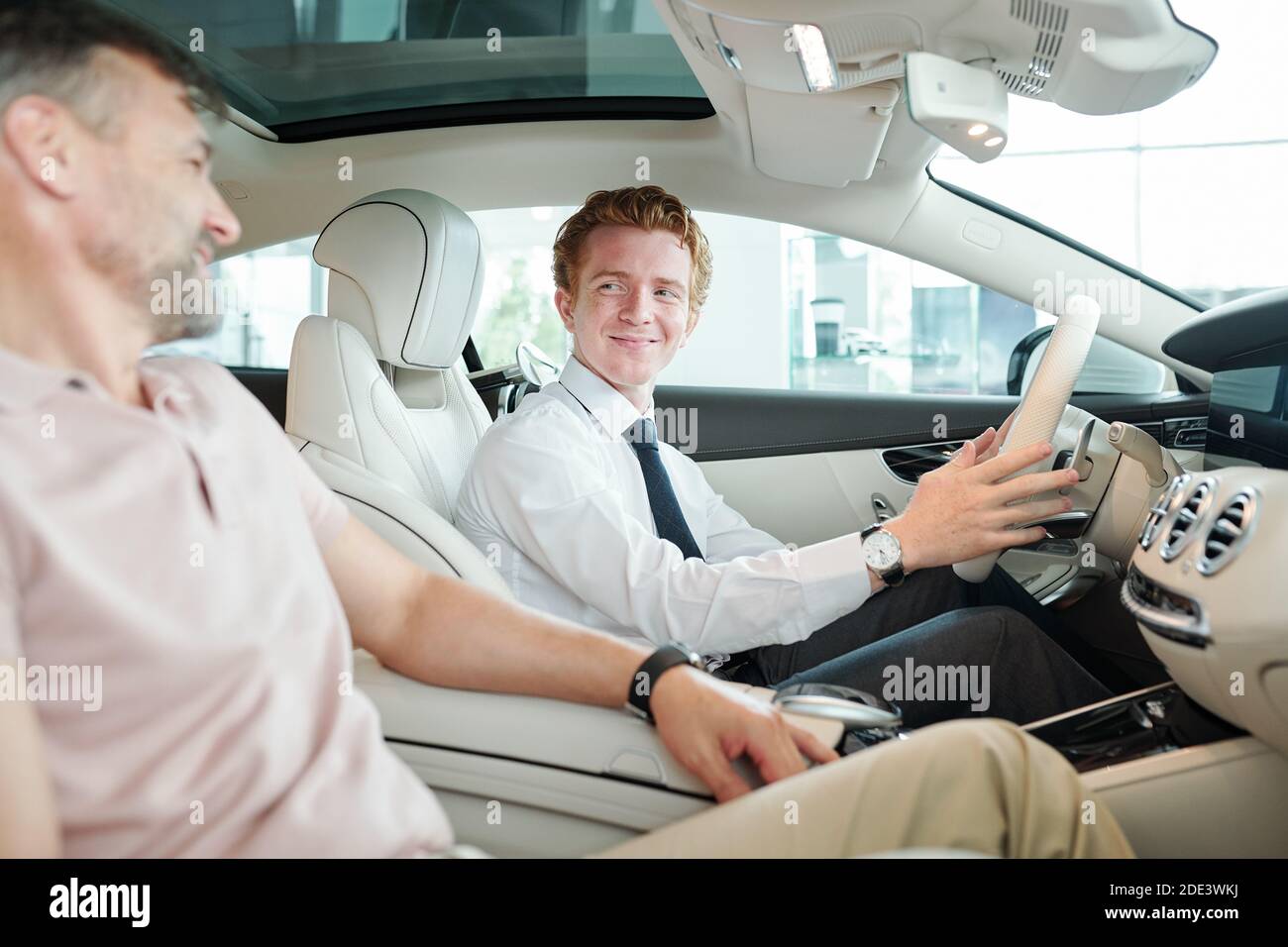 Happy young sales manager in formalwear sitting in new car and holding ...
