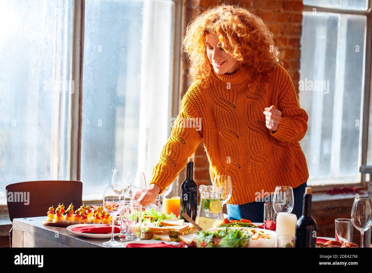Happy curly woman serving festive holiday table for feasting family ...
