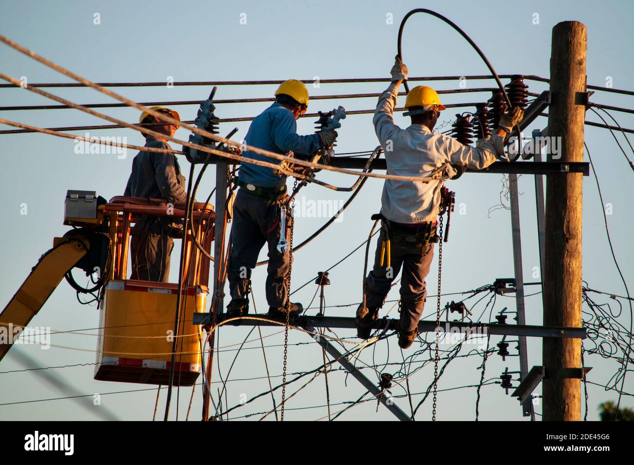 Three electric linemen working at heights on the street cables, one on ...