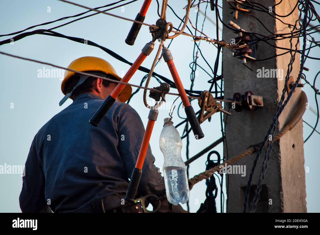 Electric lineman in a yellow helmet working with clamps at heights on ...