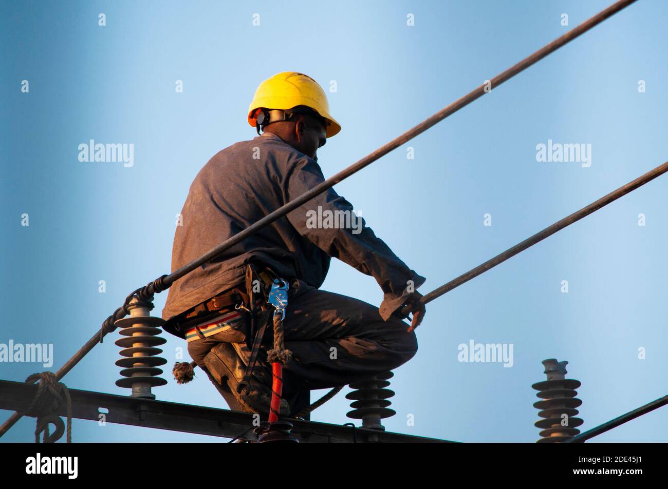 Electric lineman in a yellow helmet working with clamps at heights on ...