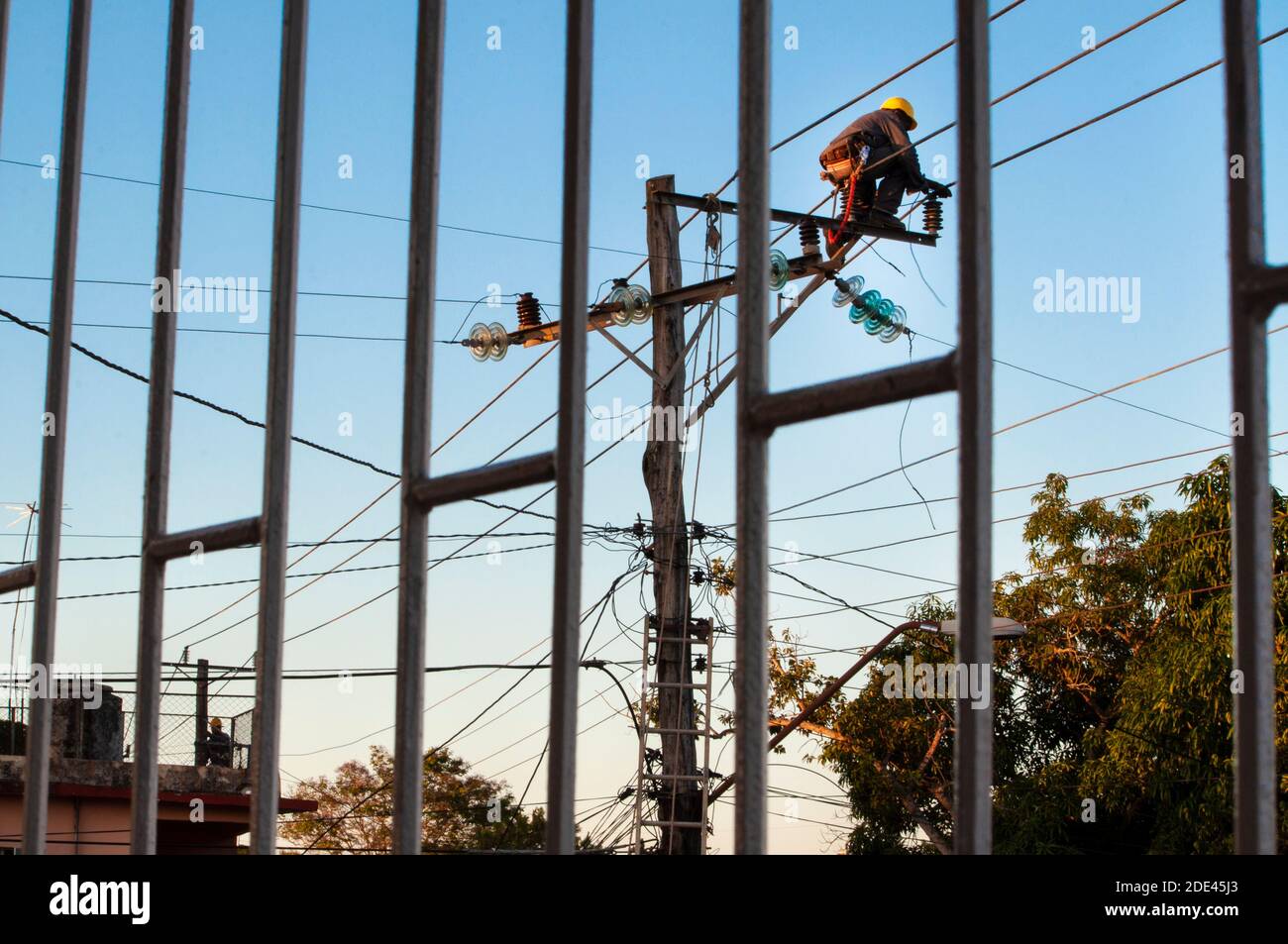 View through a fence of some electric linemen in yellow helmets working ...