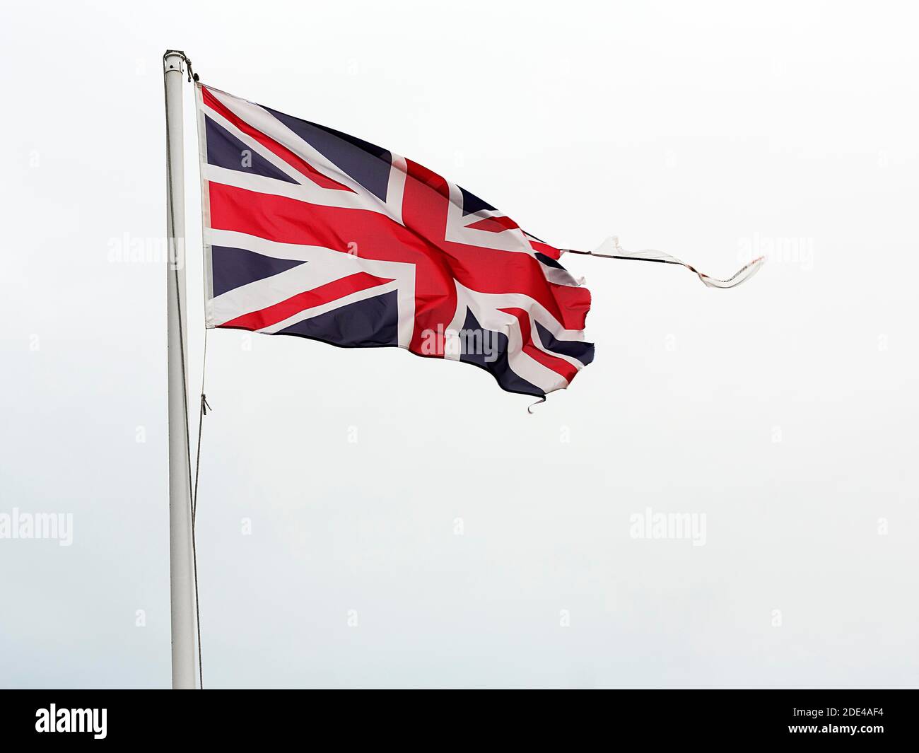 Torn British flag, Union Jack in front of grey sky, fluttering on the ...
