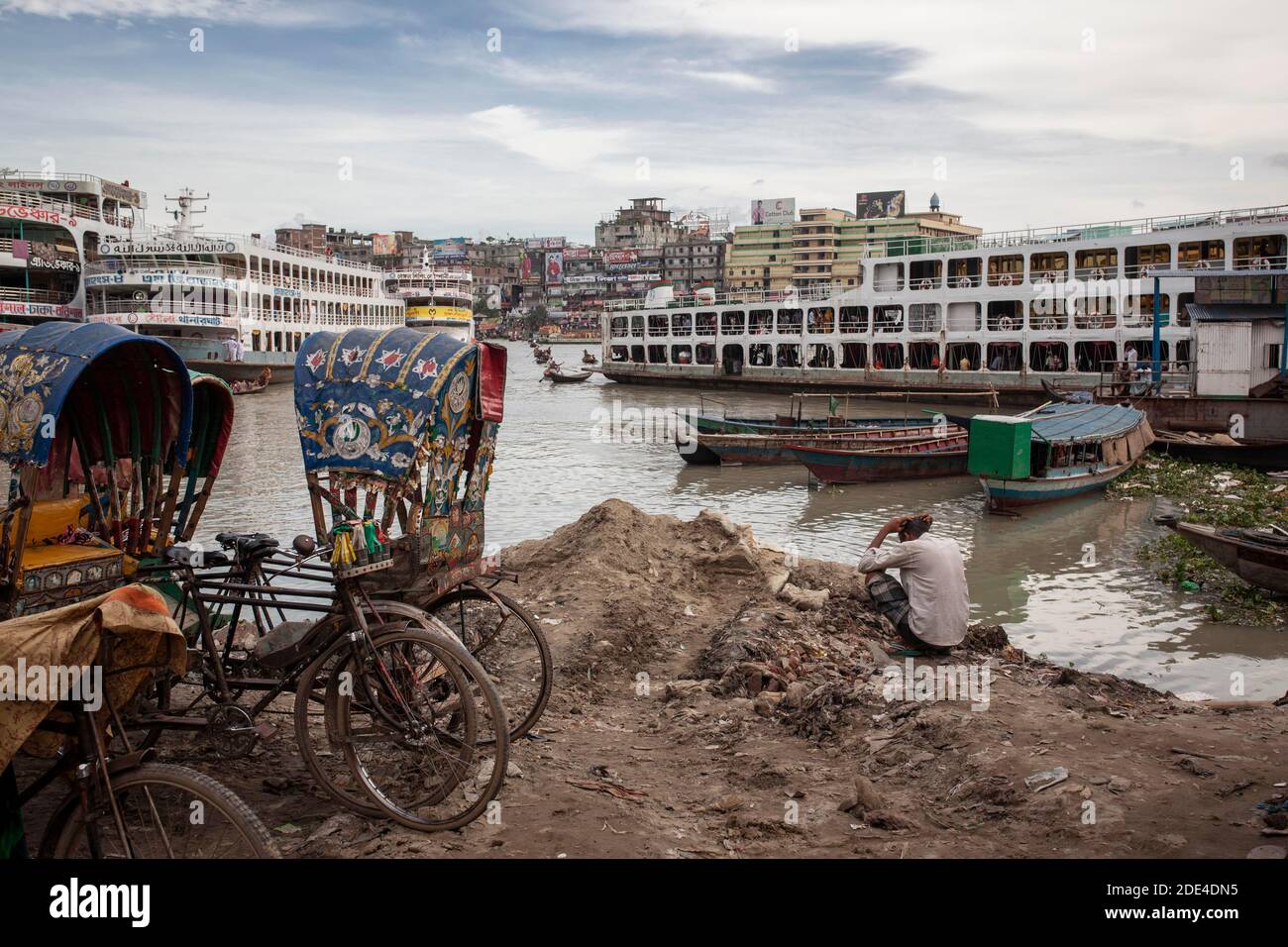 Man at prayer, rickshaws, harbour, behind it boats and river ferries ...