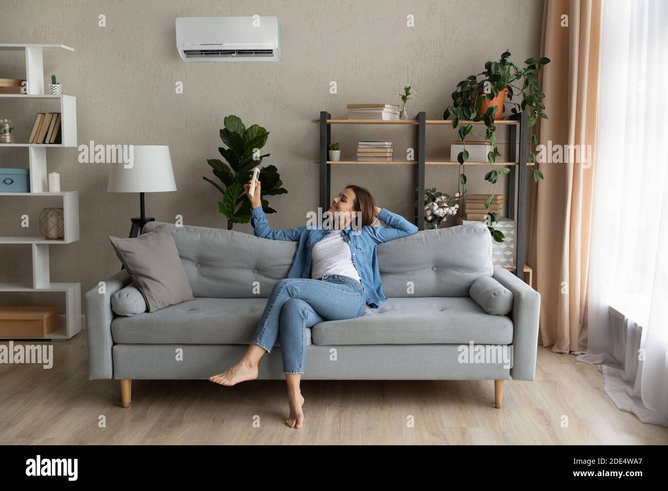 Young woman relax on couch turn on AC Stock Photo - Alamy