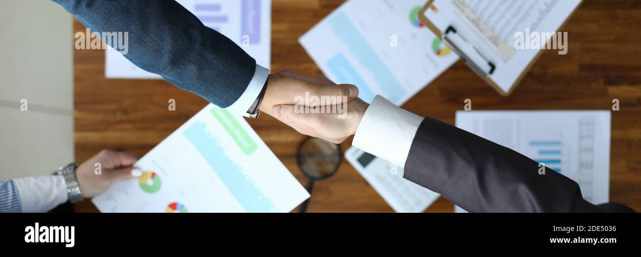 Men shake hands over the table with reports Stock Photo - Alamy
